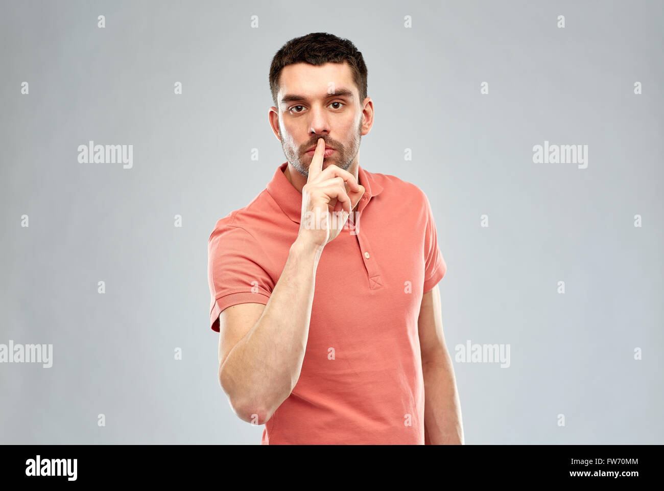 young man making hush sign over gray background Stock Photo - Alamy