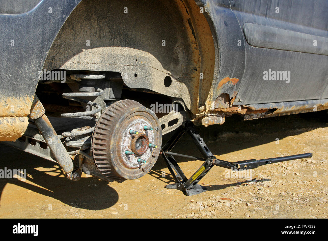 An old rusty automobile is lifted up on a jack with the wheel removed ...