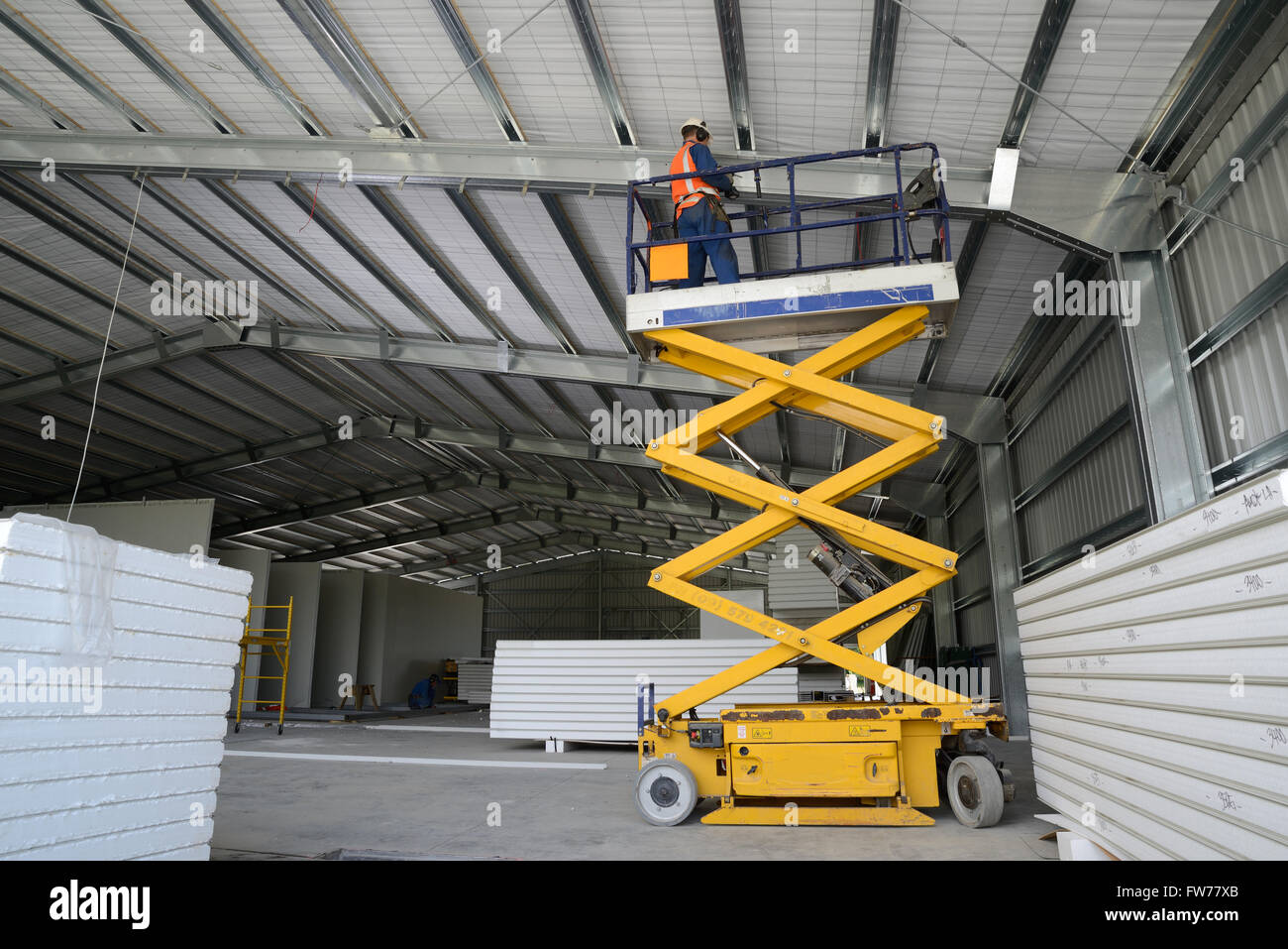 A builder works from the cage on a scissor lift while attaching beams ...