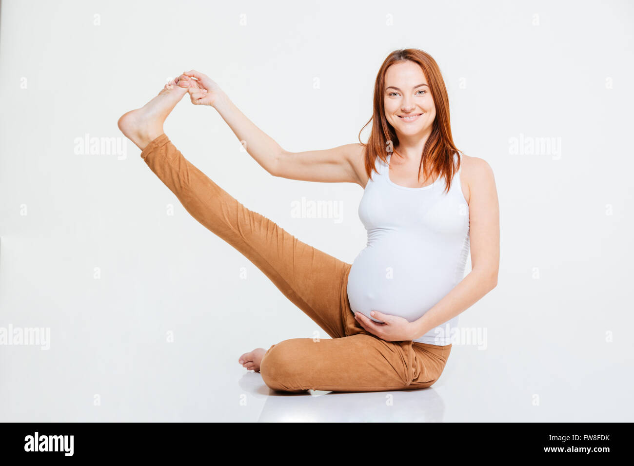 Smiling pregnant woman stretching leg on the floor isolated on a white ...