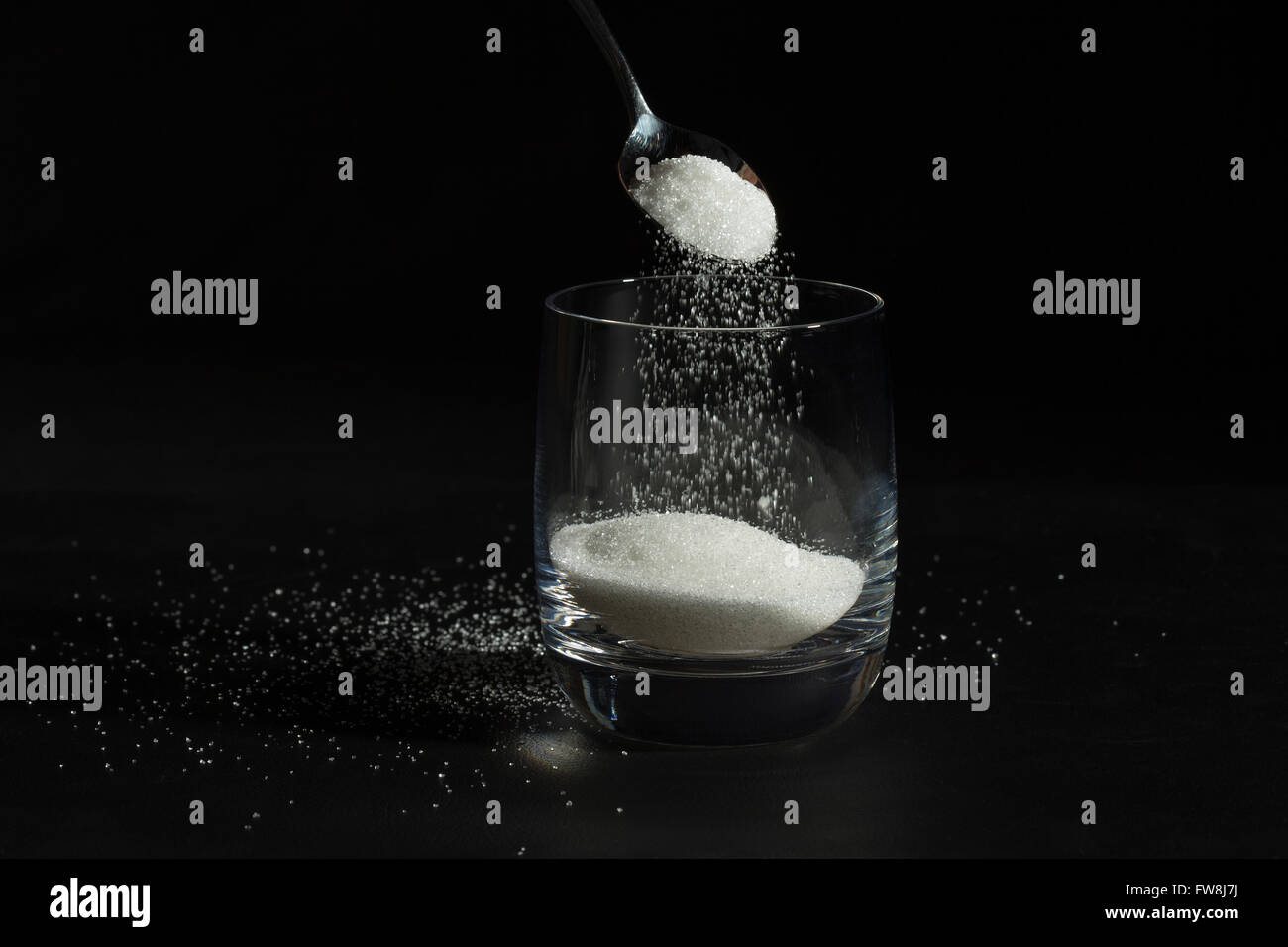 Sugar falling from a spoon into a glass, possibly demonstrating the ...