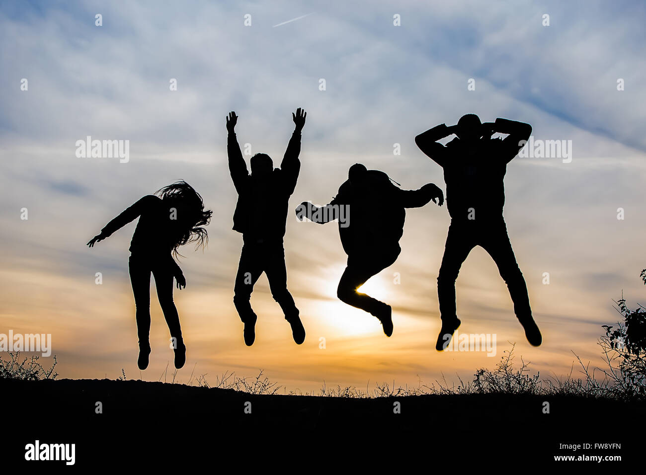 silhouette of a group of four happy people jumping at sunset, happy ...