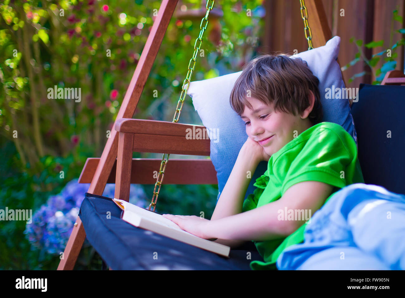 Happy school boy reading a book in the backyard. Child relaxing in a ...