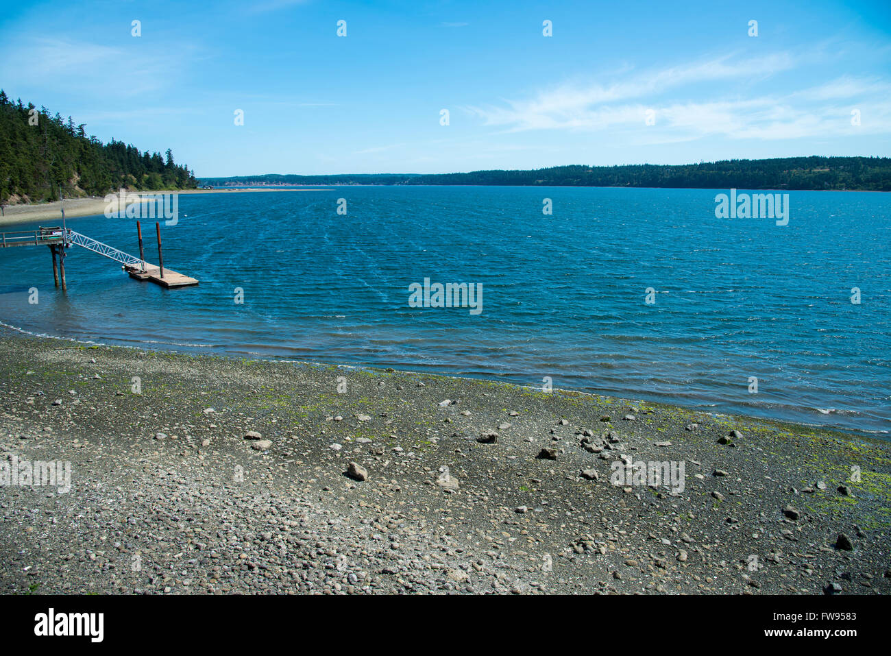 Rocky shore with boat dock on lake, blue sky and trees along shoreline ...
