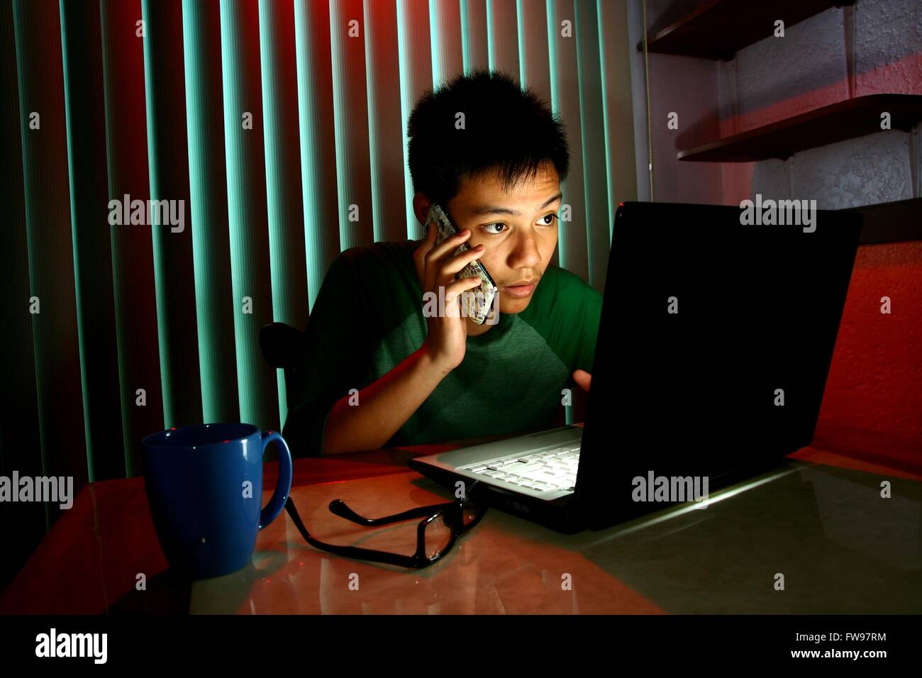 Teen using a cellphone or smartphone in front of a laptop computer ...