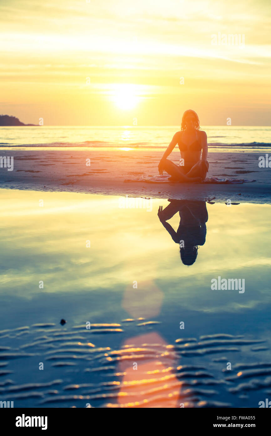 Female silhouette with reflection in water, meditation pose at sunset ...