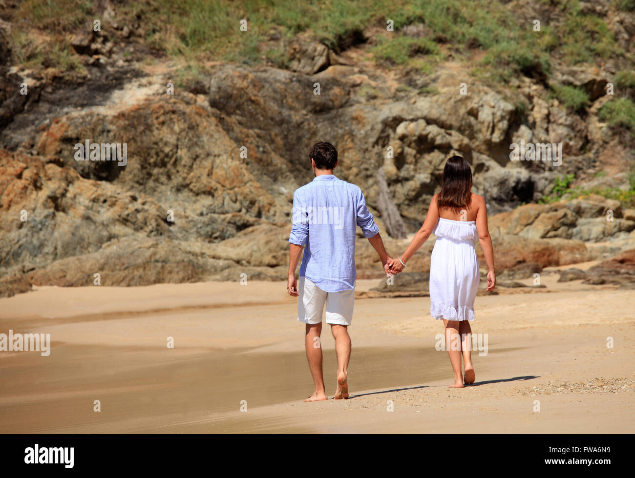 Cheerful couple walking on beach on rock background Stock Photo - Alamy