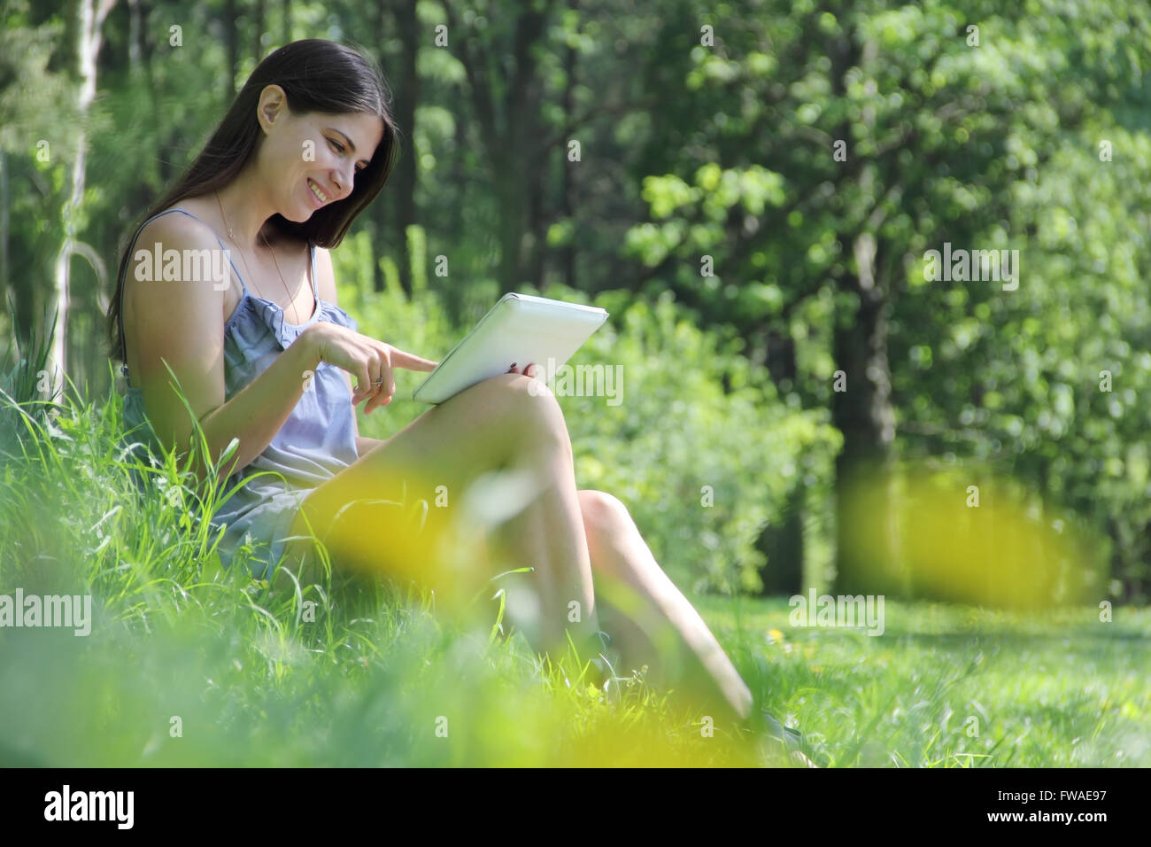 Young woman using tablet outdoor sitting under tree in park Stock Photo ...