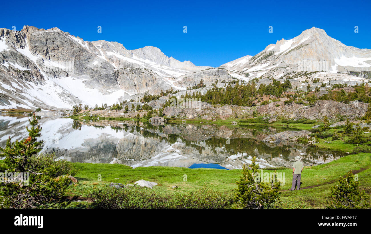 Hiker looks at peaks reflected in lake at 20 Lakes Basin in the Eastern ...