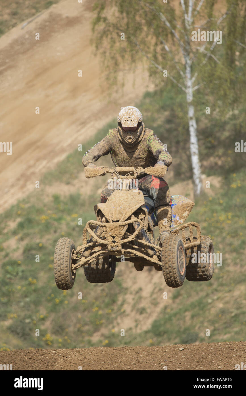 Quad racer is high jumping. The quad bike and rider are very muddy ...