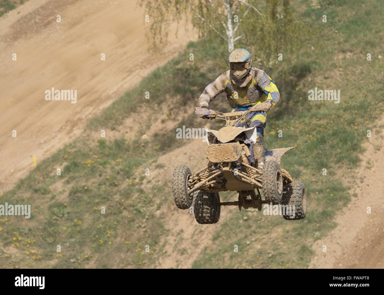 Quad racer is high jumping. The quad bike and rider are very muddy ...