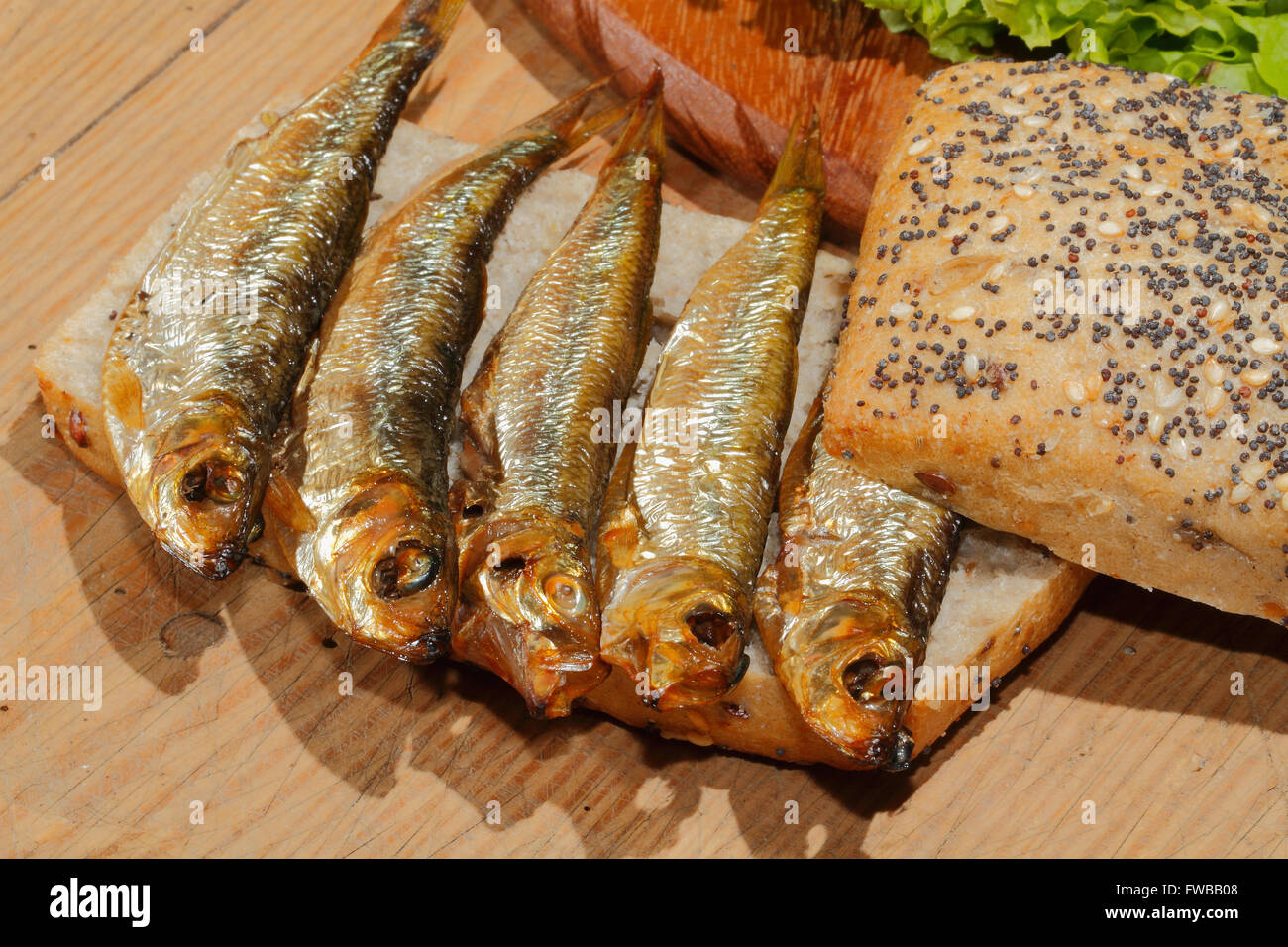 Smoked sprat in whole wheat bread, with lettuce on a wooden chopping ...