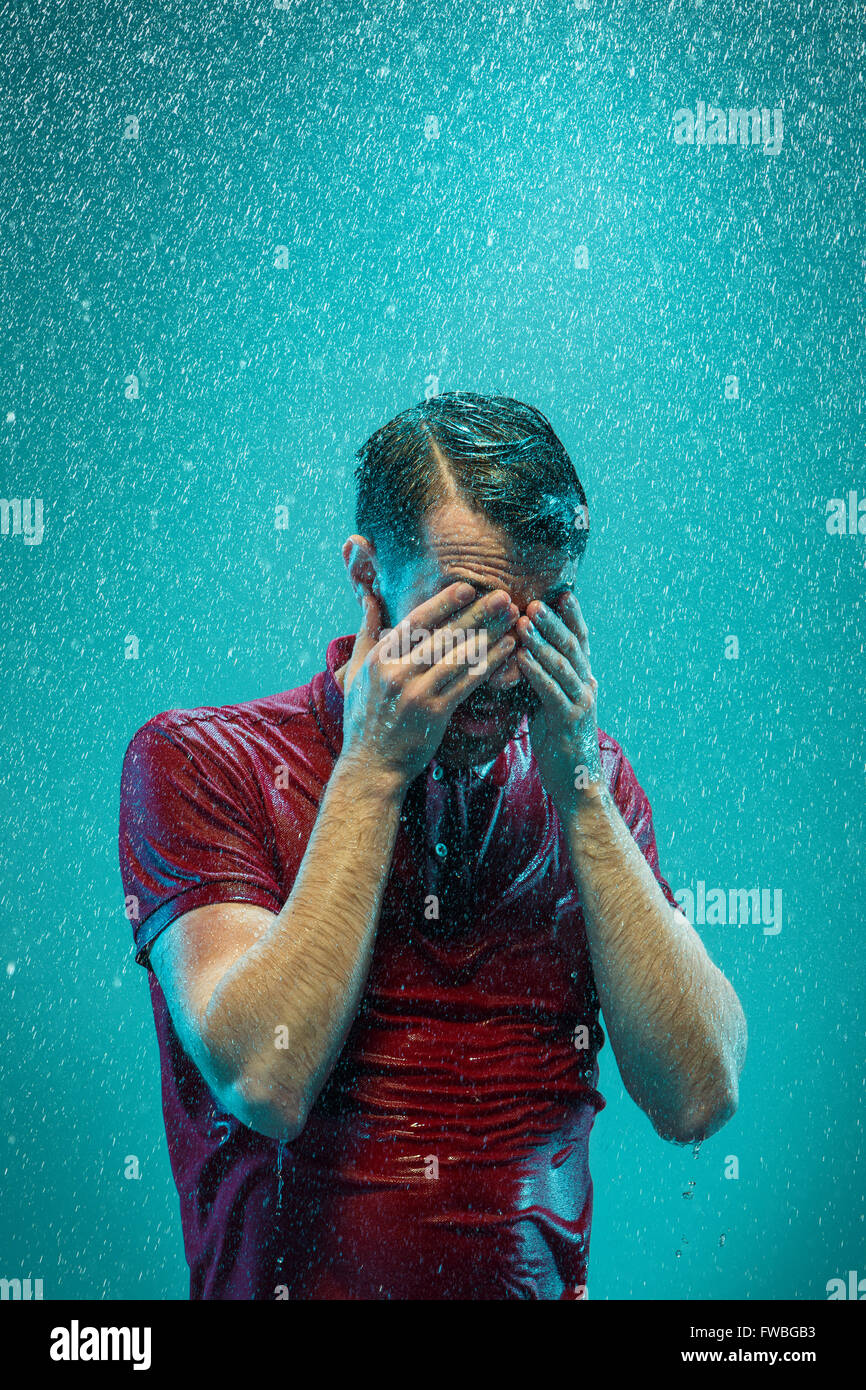 The portrait of young man in the rain. The man standing on a turquoise ...