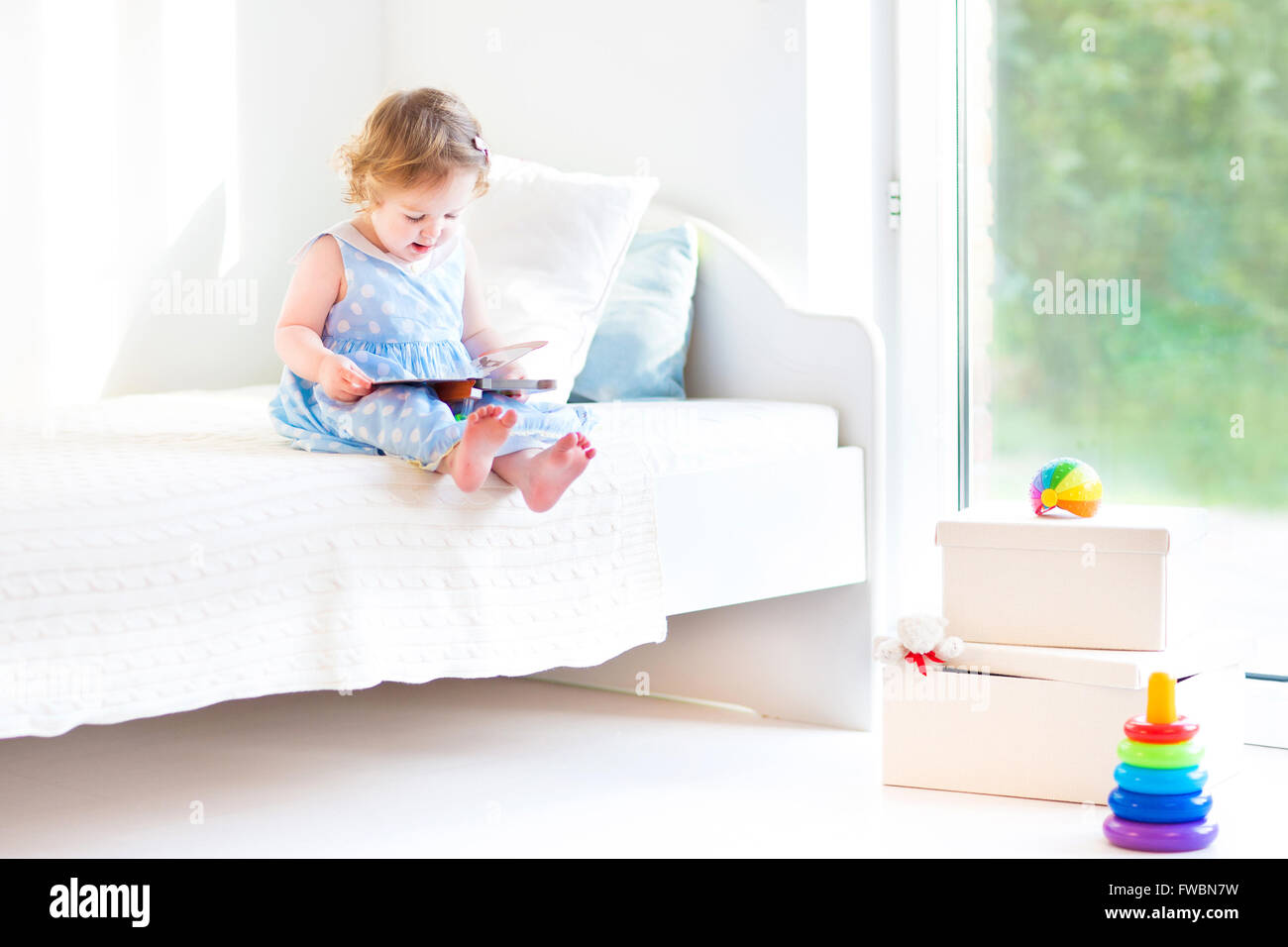 Funny happy toddler girl reading a book and playing with her toy teddy ...