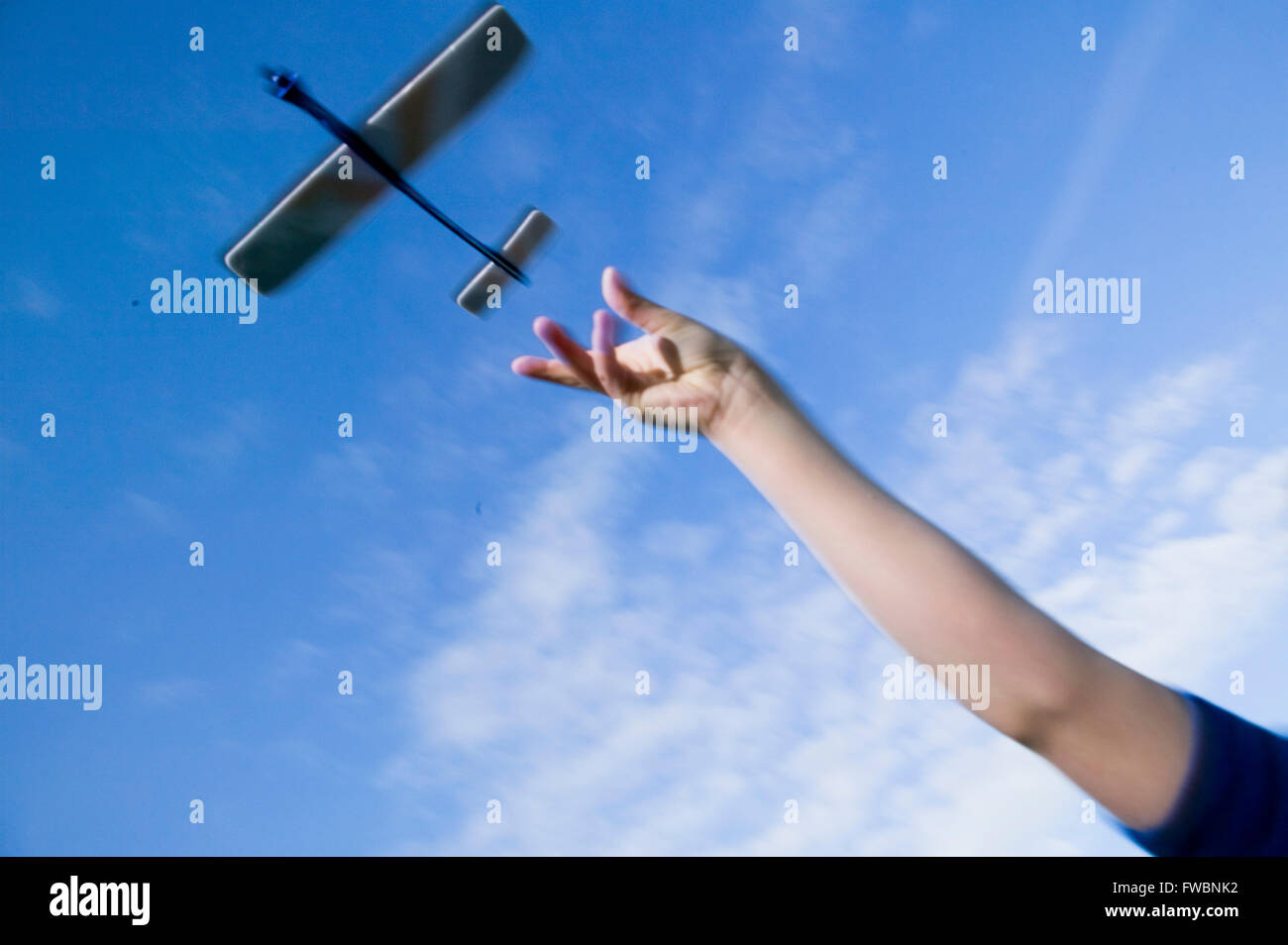 Model or paper aeroplane being launched inot the sky with clouds as the ...
