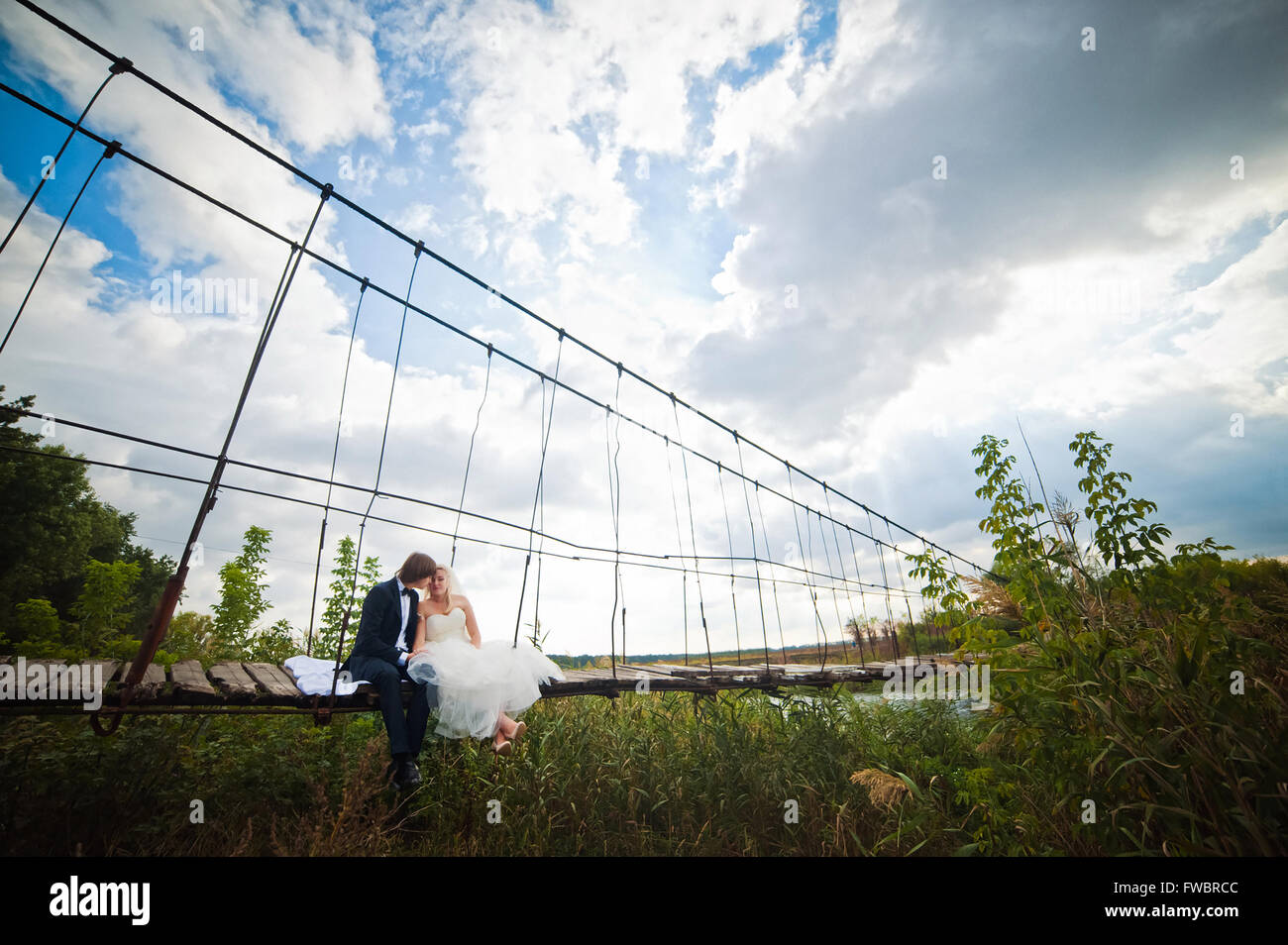 groom and bride sitting on bridge Stock Photo - Alamy