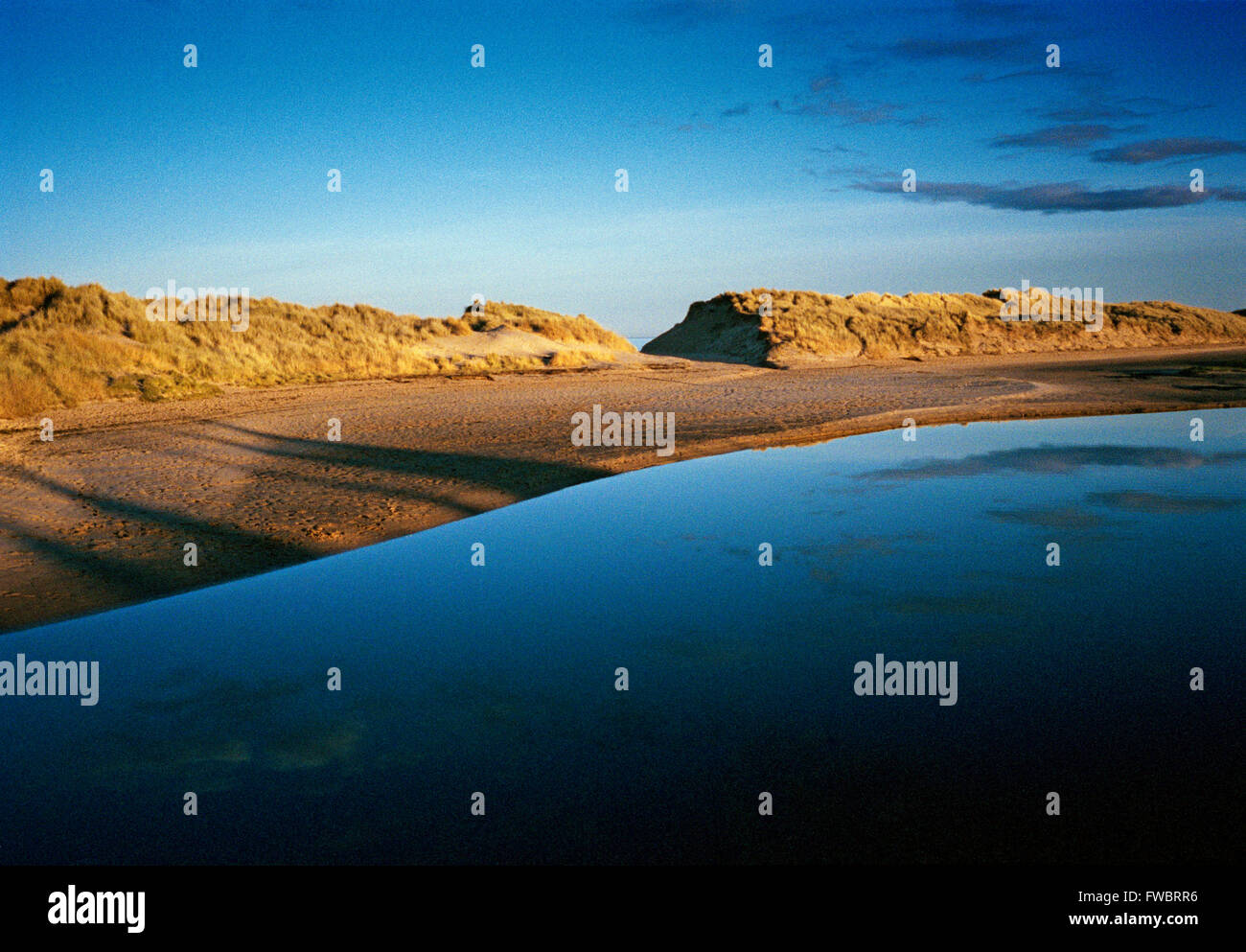 The reflection of sand dunes appears in the dark waters of a scottish ...