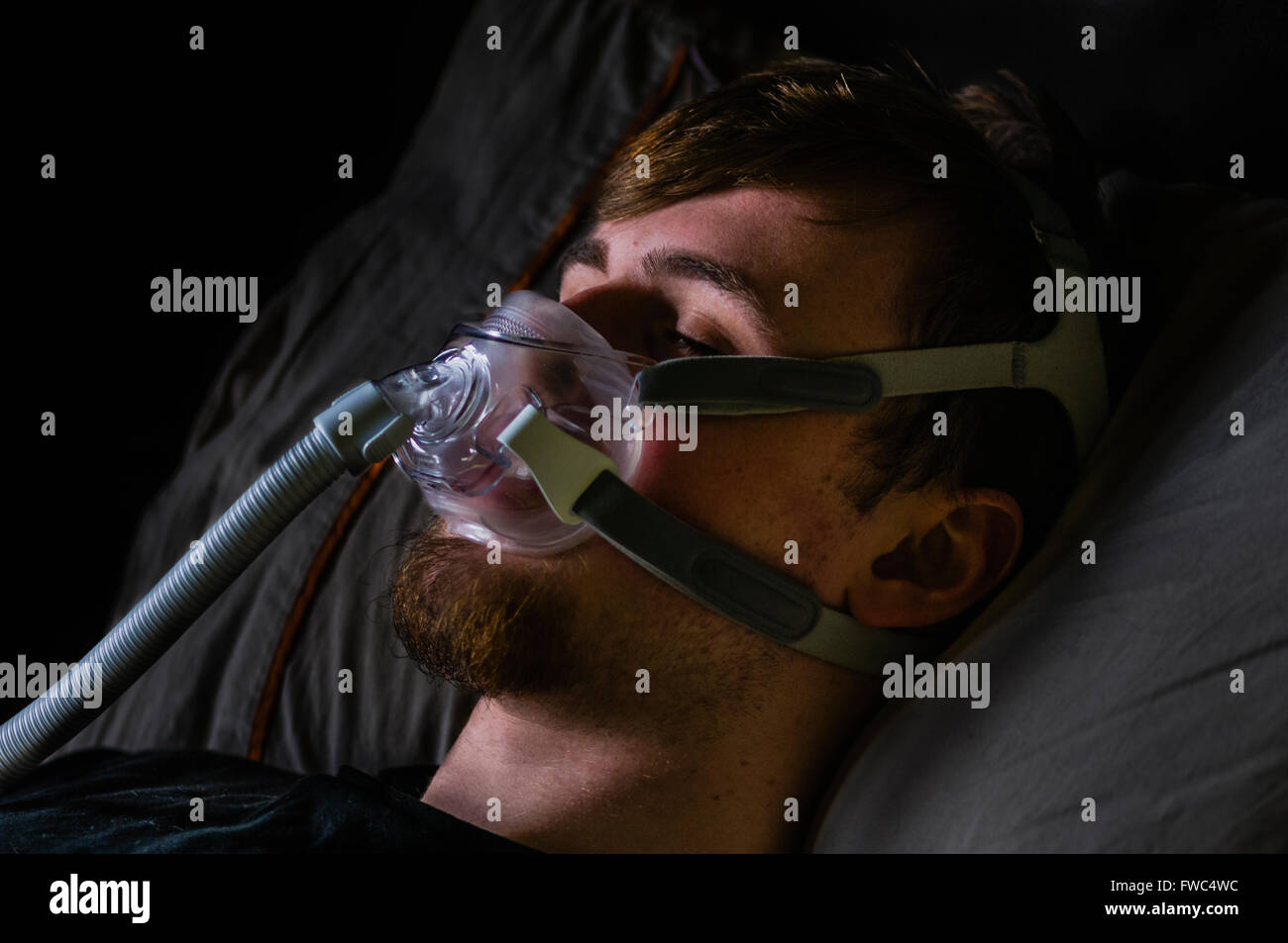 A man in bed at night using a Philips Respironics System One CPAP ...