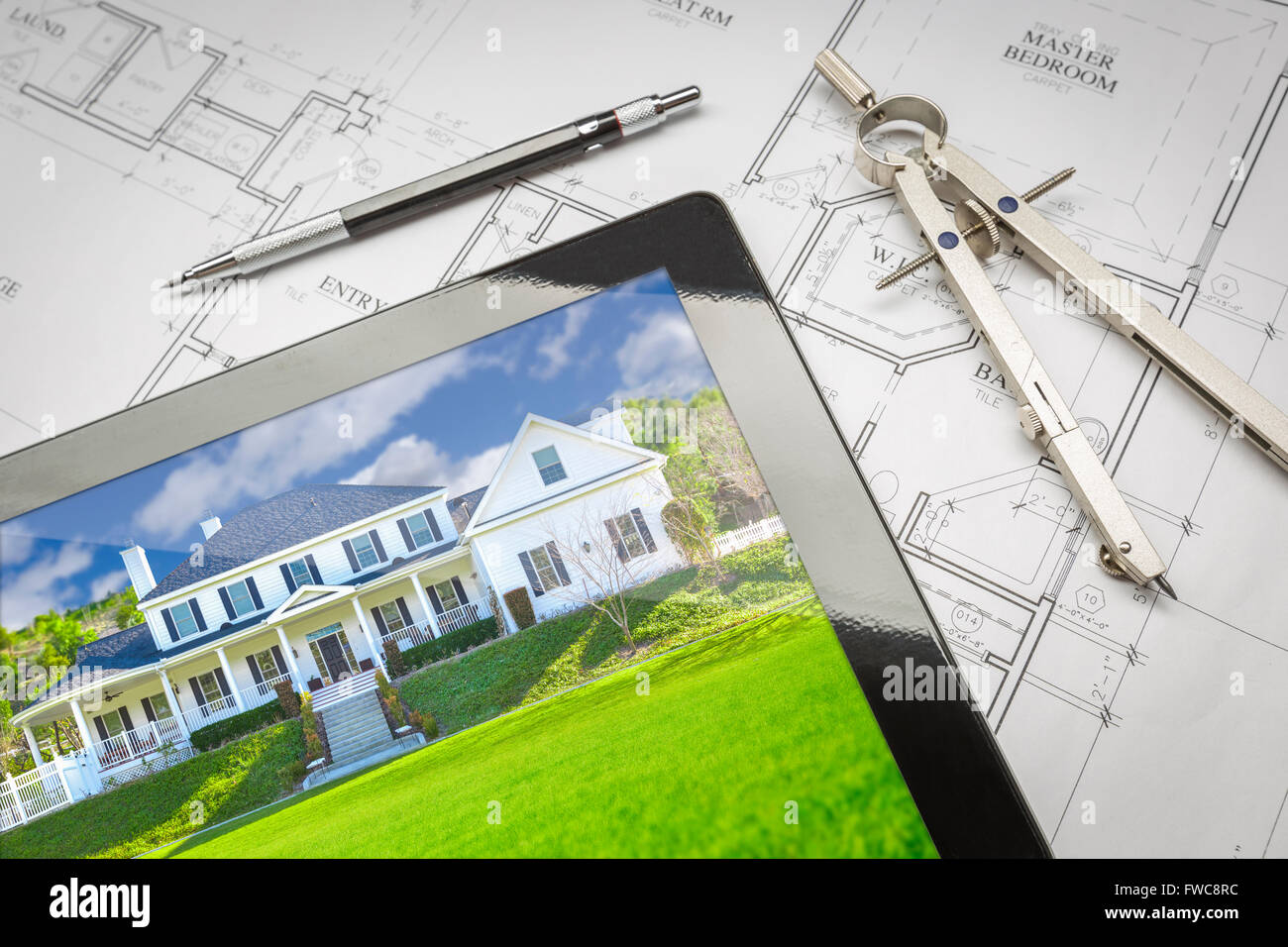 Computer Tablet Showing Finished House Sitting On House Plans With ...