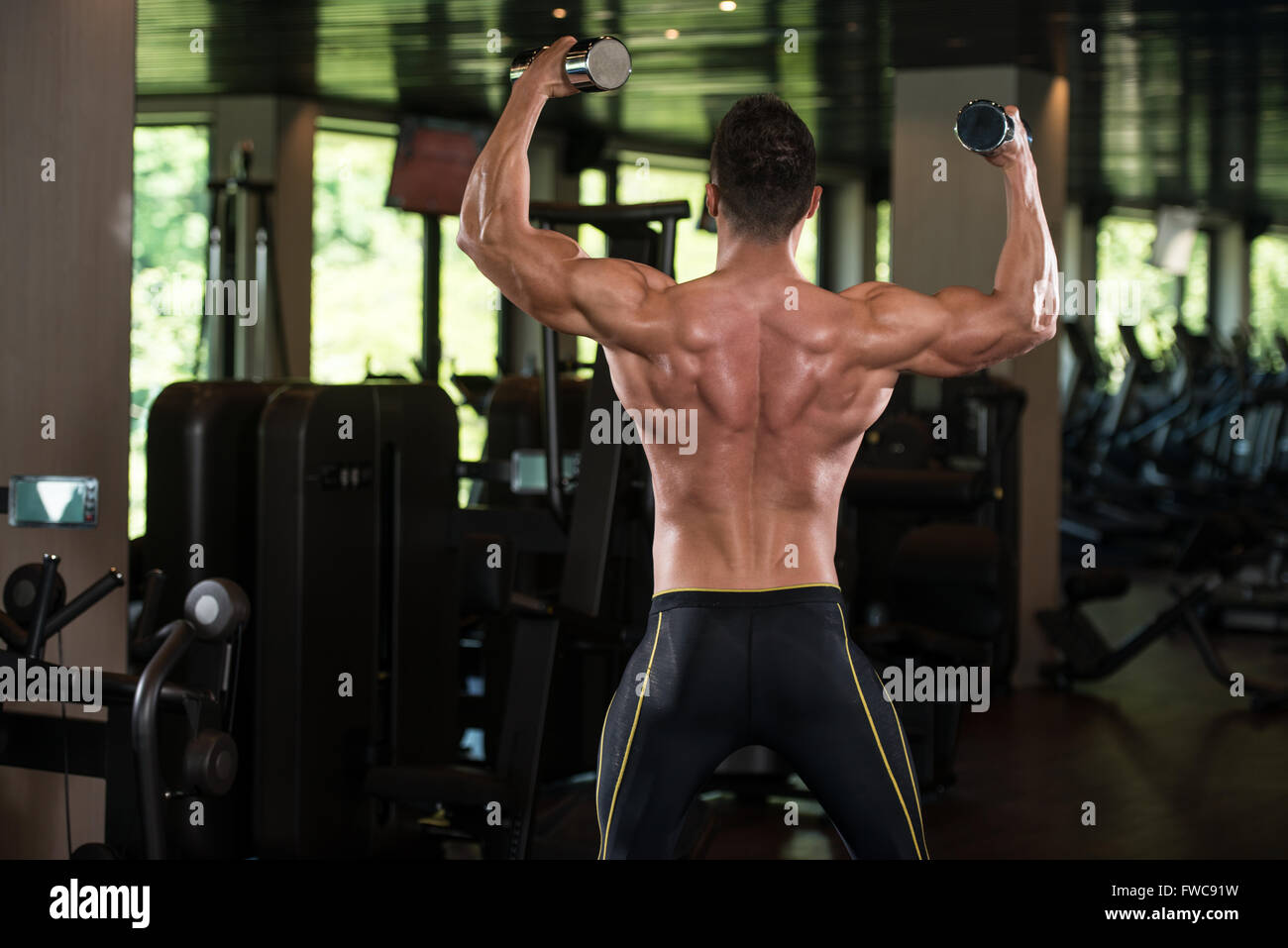 Portrait Of A Physically Fit Man Posing With Dumbbells In Modern ...