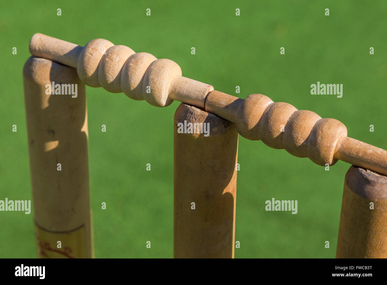 Well used cricket stumps and bails set up on pitch. Grassy green ...