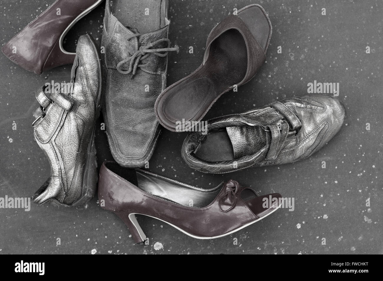 Various abandoned shoes laid on the ground, overhead shot in black and ...