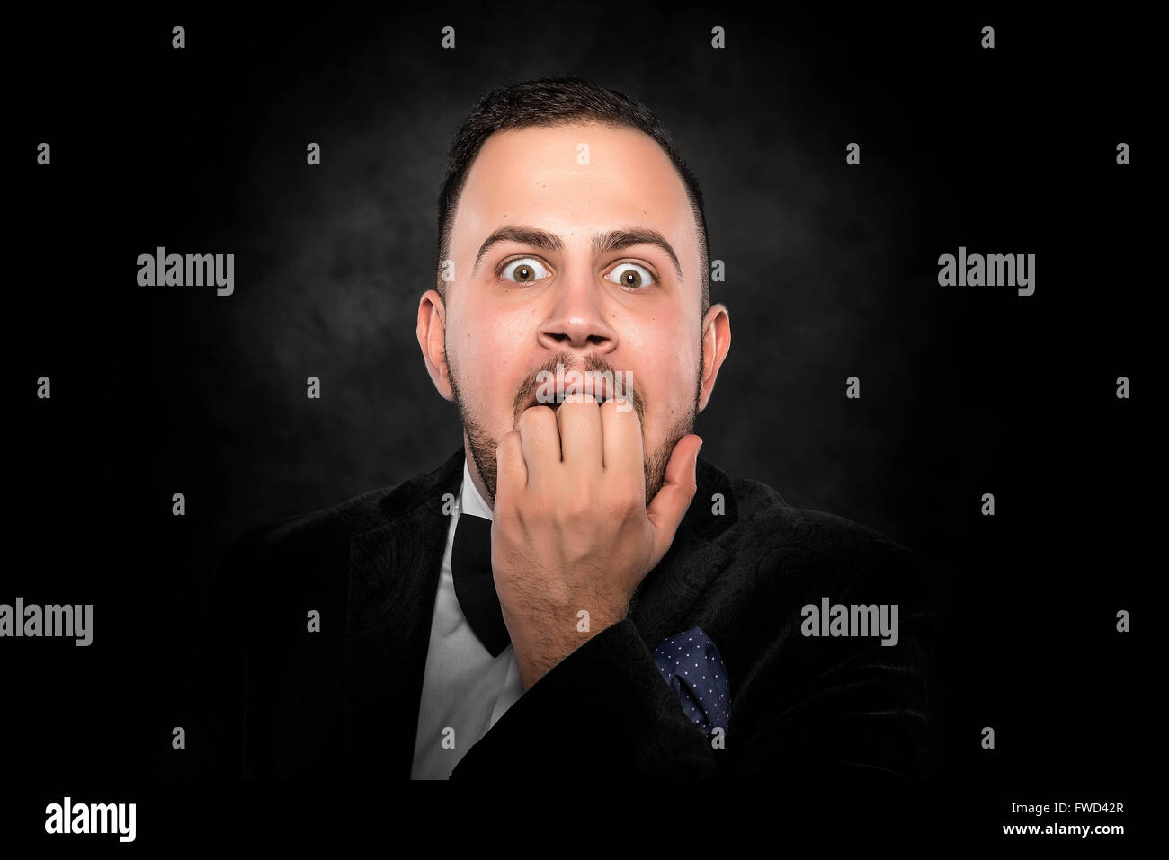 Portrait of surprised man in suit with bow-tie over dark background ...