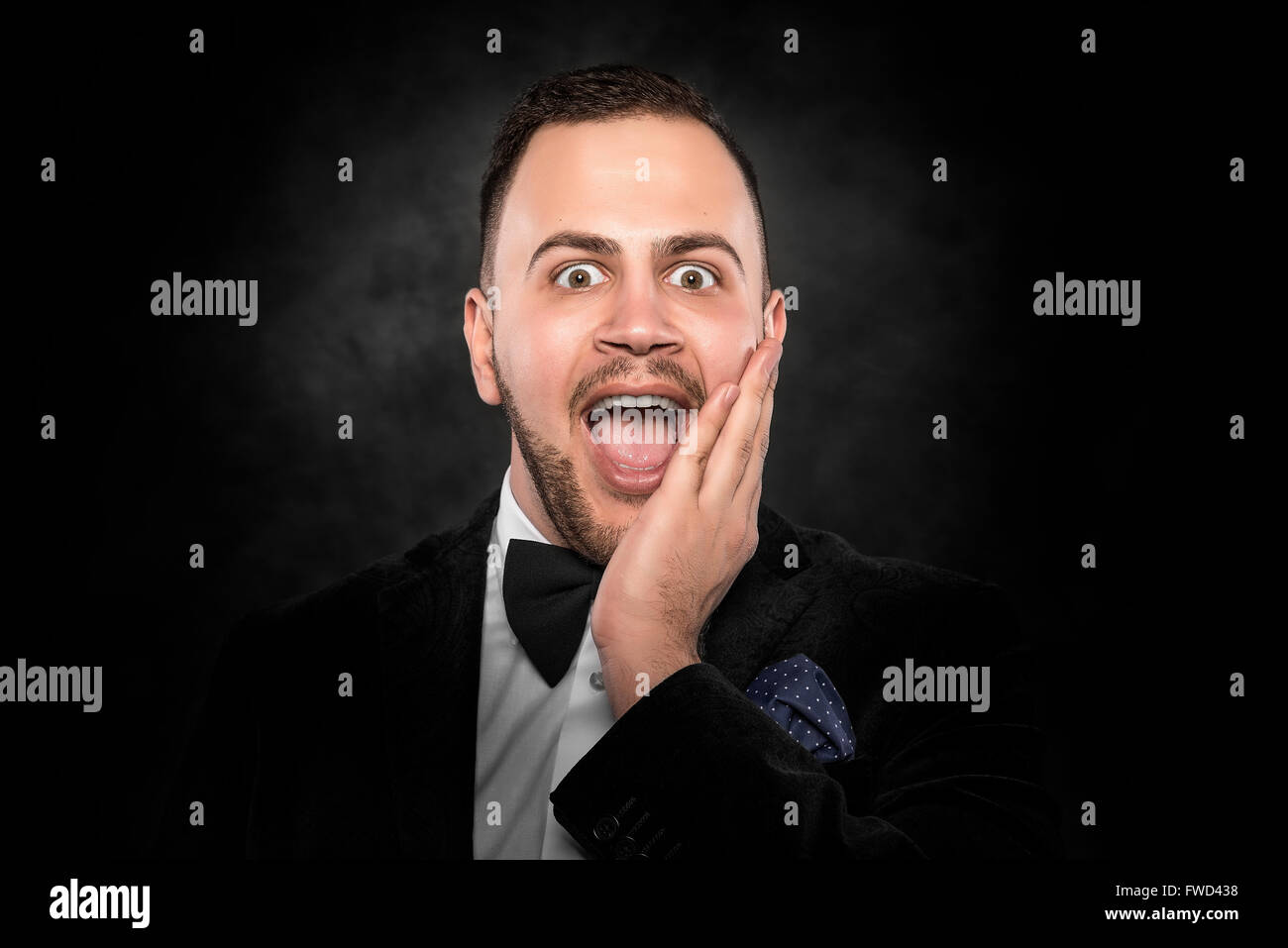 Portrait of surprised man in suit with bow-tie over dark background ...