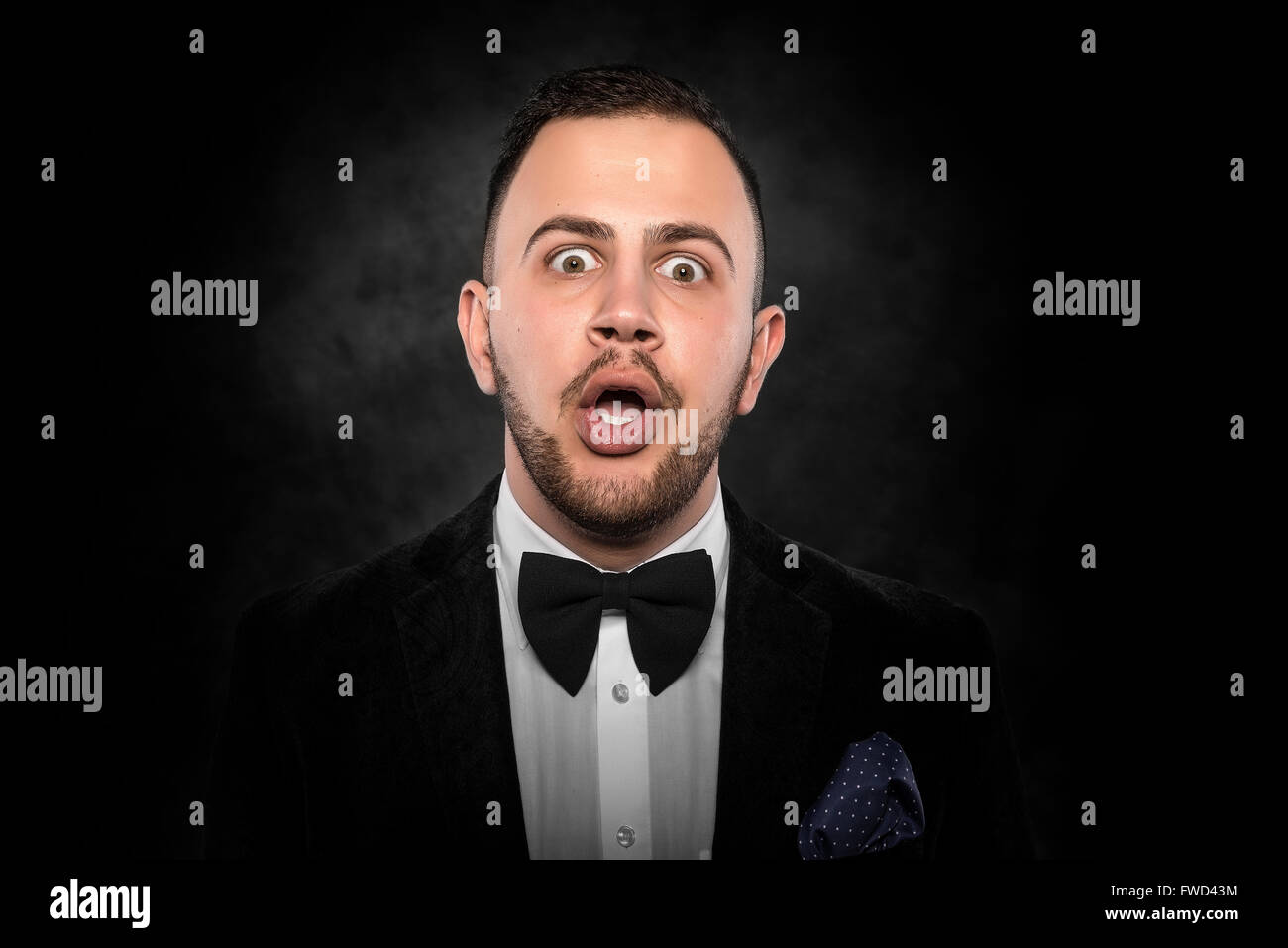 Portrait of surprised man in suit with bow-tie over dark background ...