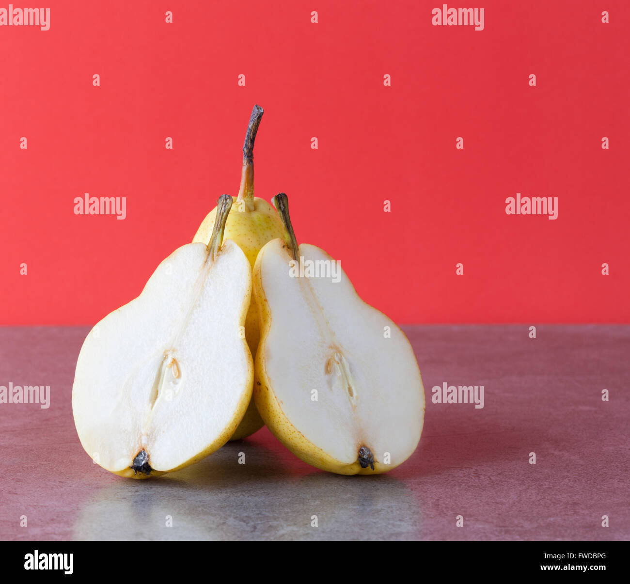 Whole and halved yellow Corella pears on red background with copy space ...