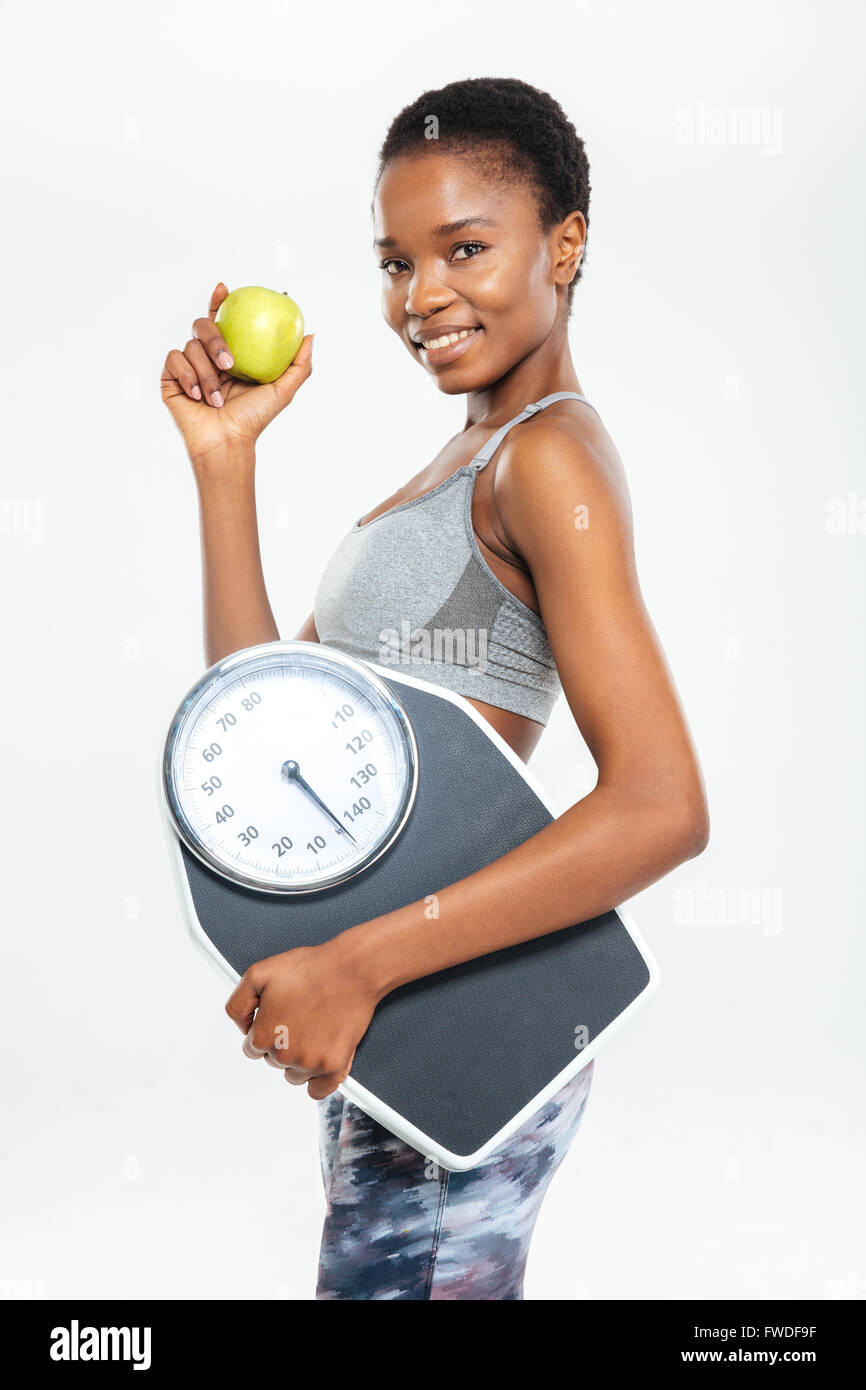 Happy afro american woman holding scales and apple isolated on a white ...