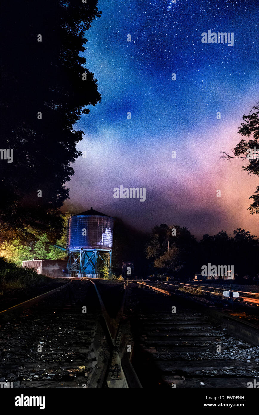 An atmospheric fog pours over a water tower, enclosing the starry skies ...
