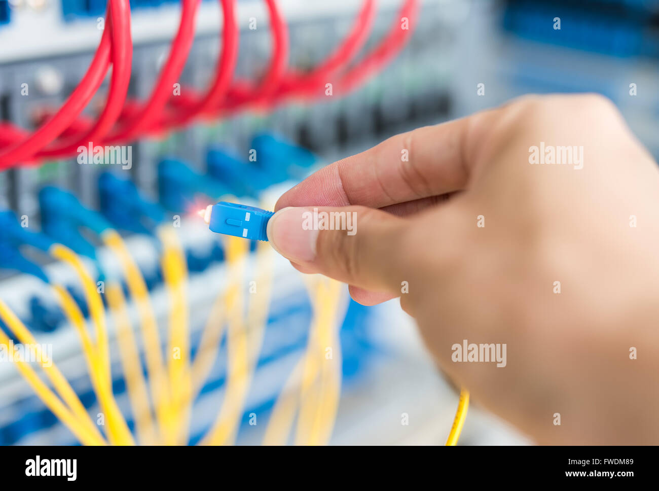 man working in network server room with fiber optic hub for digital ...