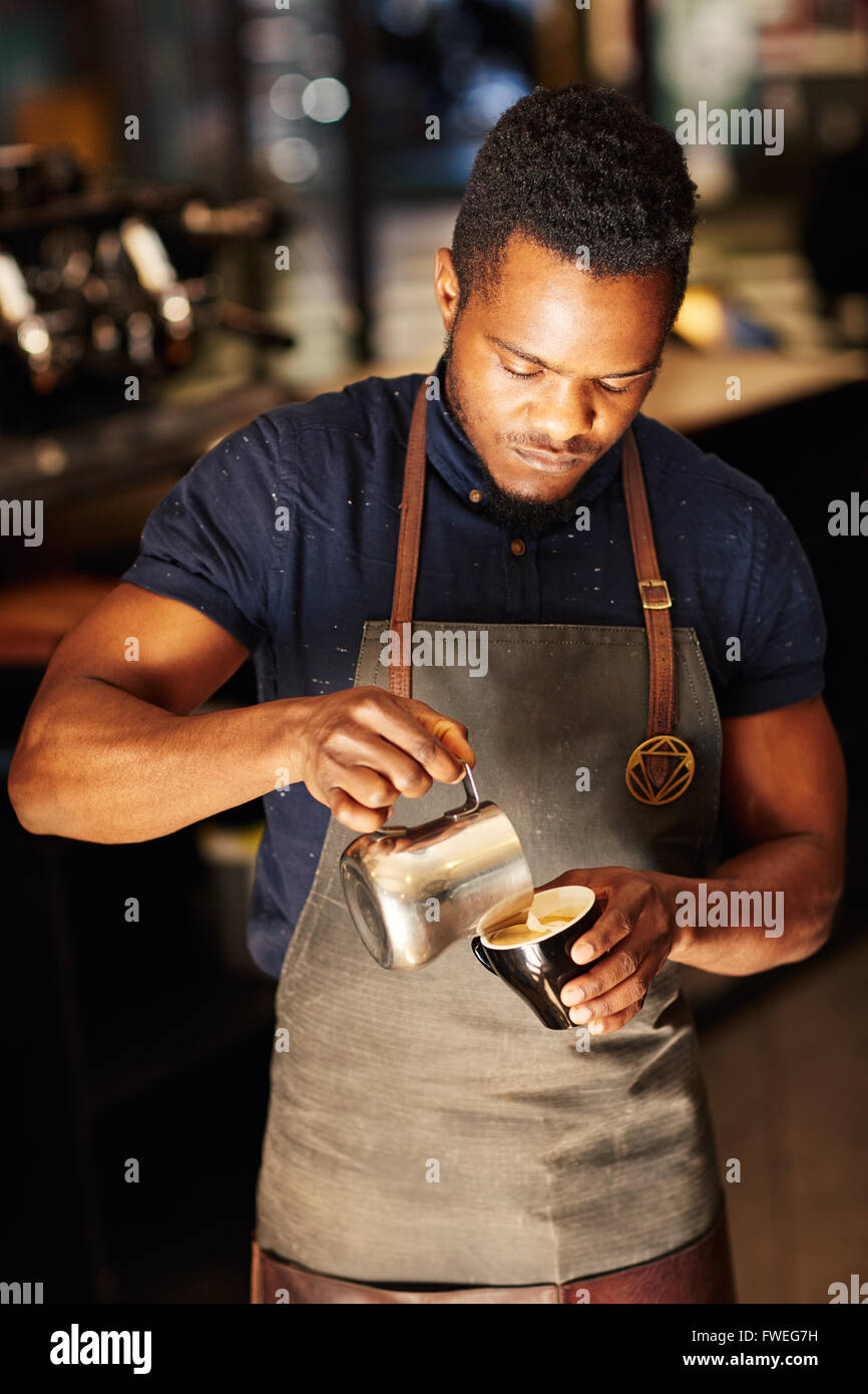 High angle view of a handsome African man carefully pouring frothy milk ...