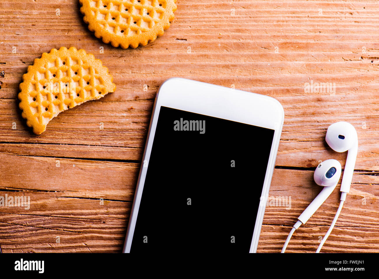 Smartphone, earphones and biscuits laid on old office desk Stock Photo ...