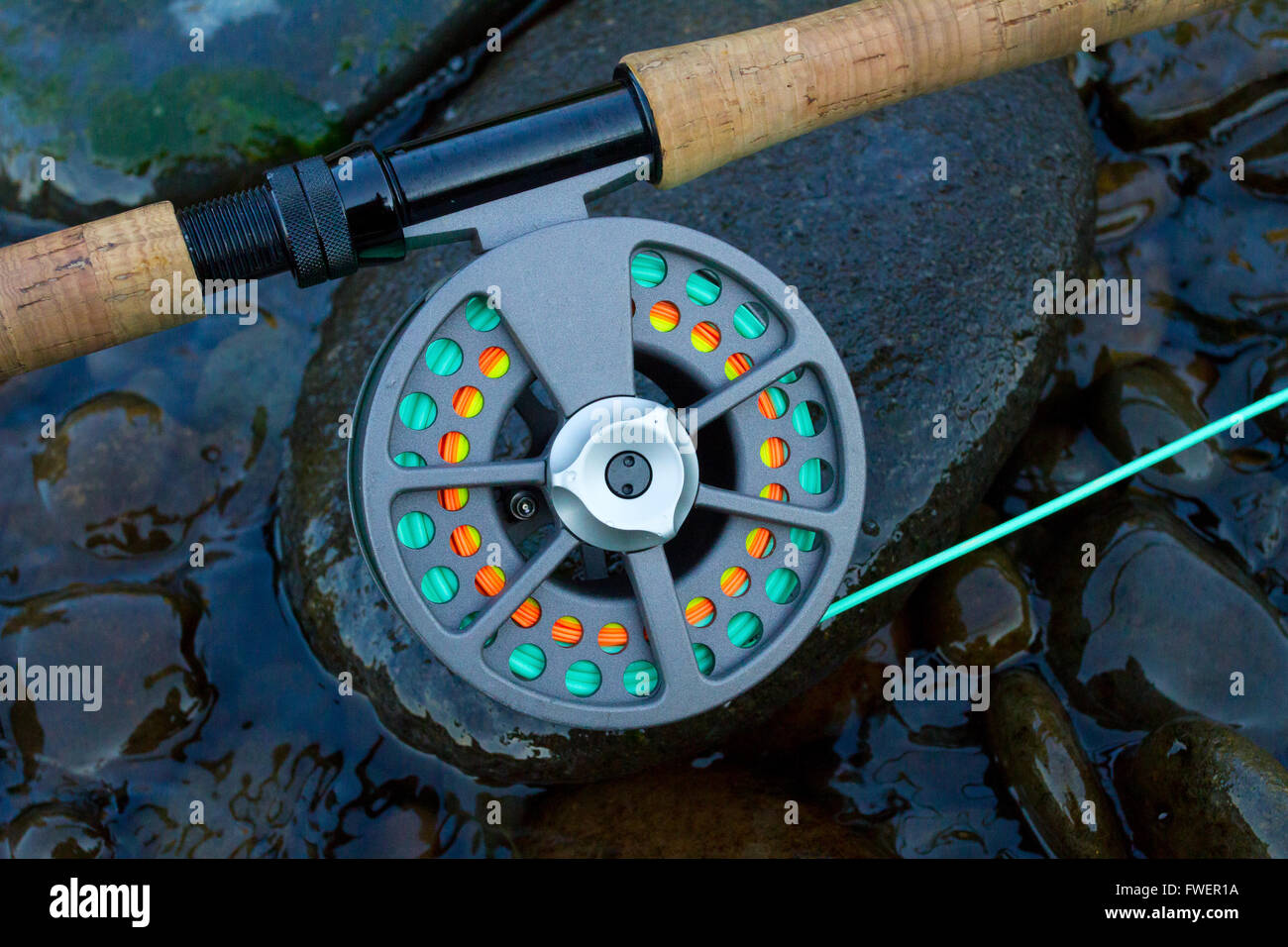 A fly fishing rod and reel sit upon some river rock on the edge of the ...