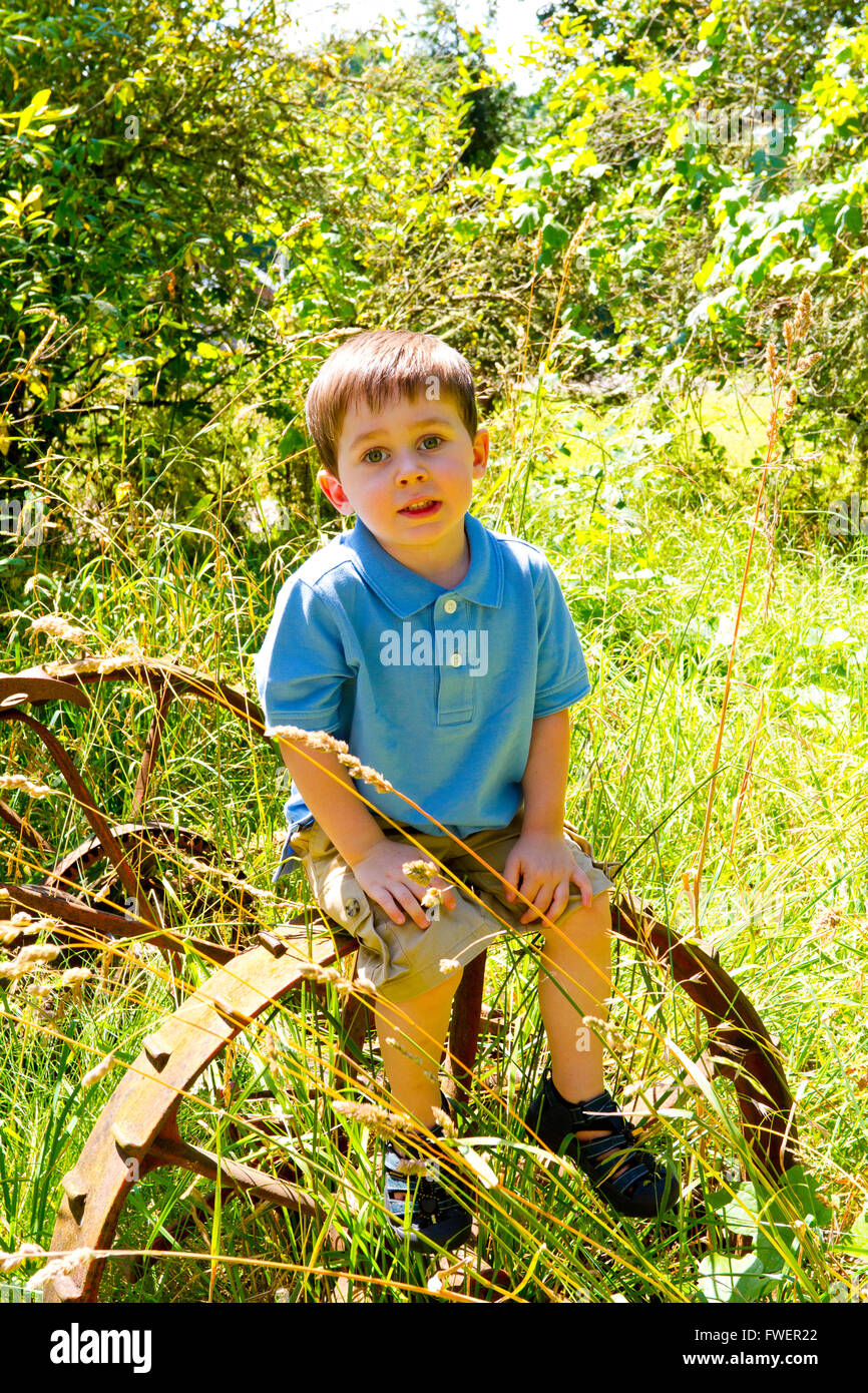 A young child is playing in a blue polo shirt near some farm equipment ...