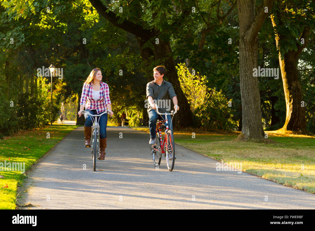 A man and a woman with their bicycles on a bike path in an outdoor park ...