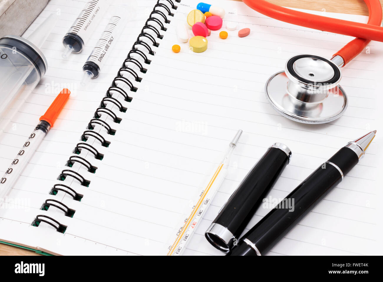 Red stethoscope, syringes, pen, and many colorful pills on blank ...