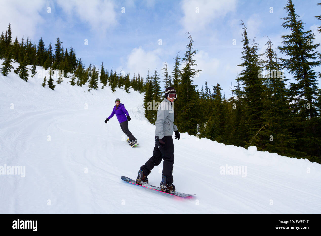 A couple snowboards down some groomed ski runs at a mountain resort ...