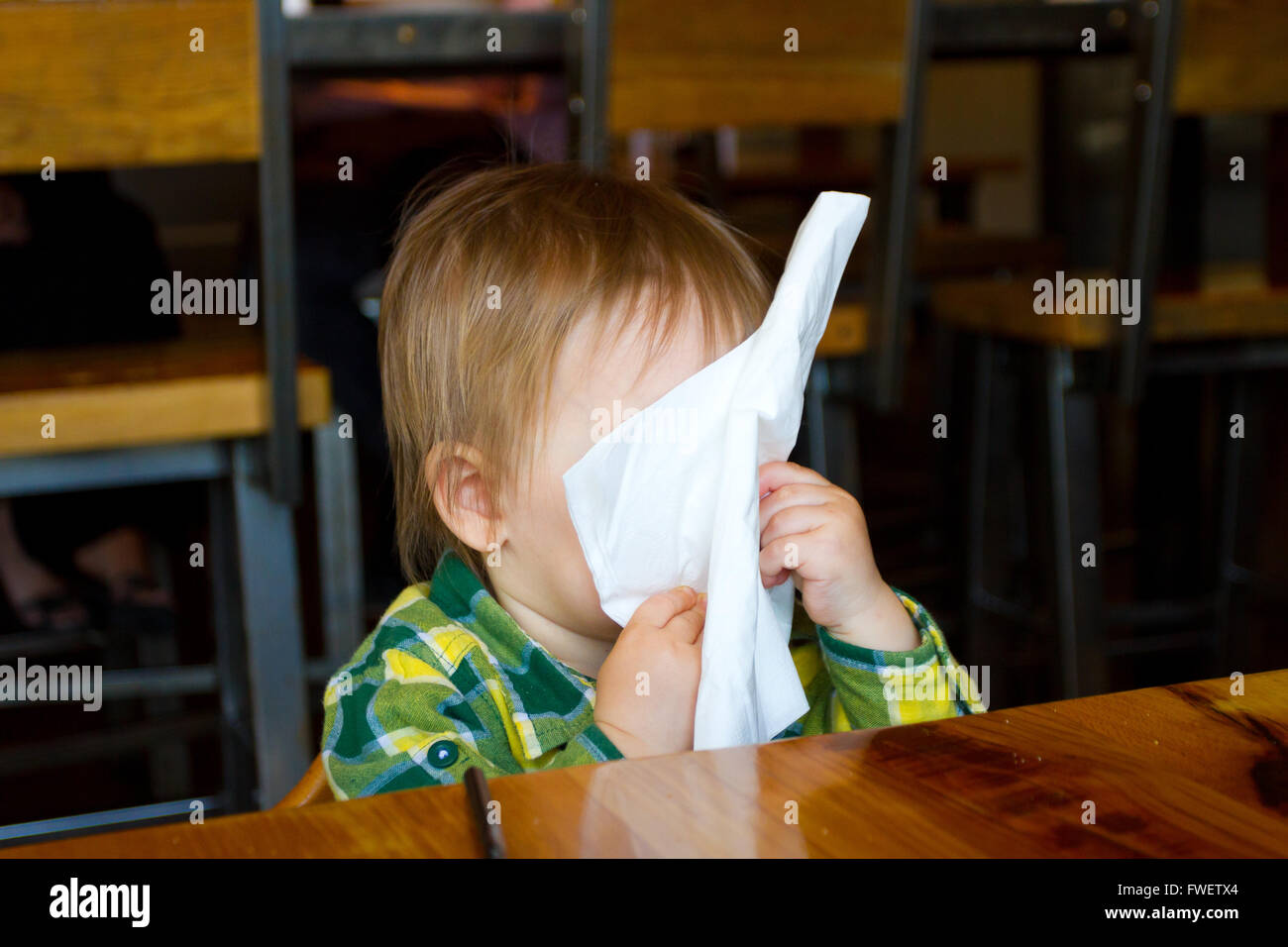 A young one year old toddler boy plays with a napkin at a restaurant ...
