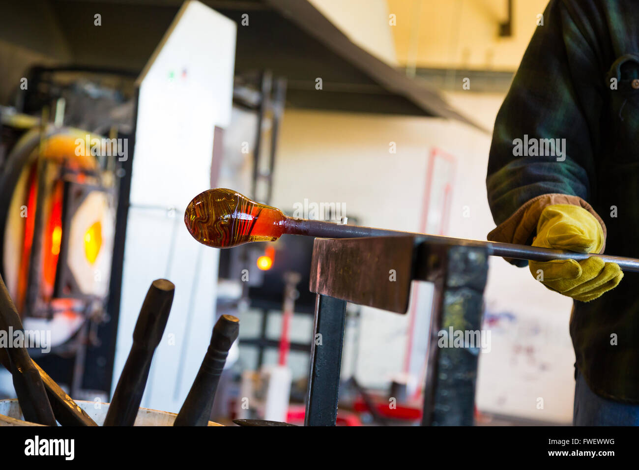 A very talented glassblower is forming and shaping glass in a studio ...