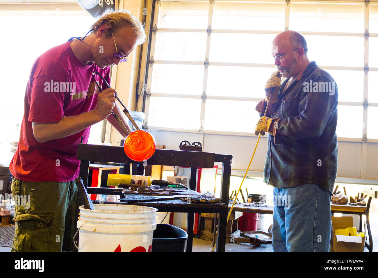 Two men are working hard to create a unique art piece of molten glass ...
