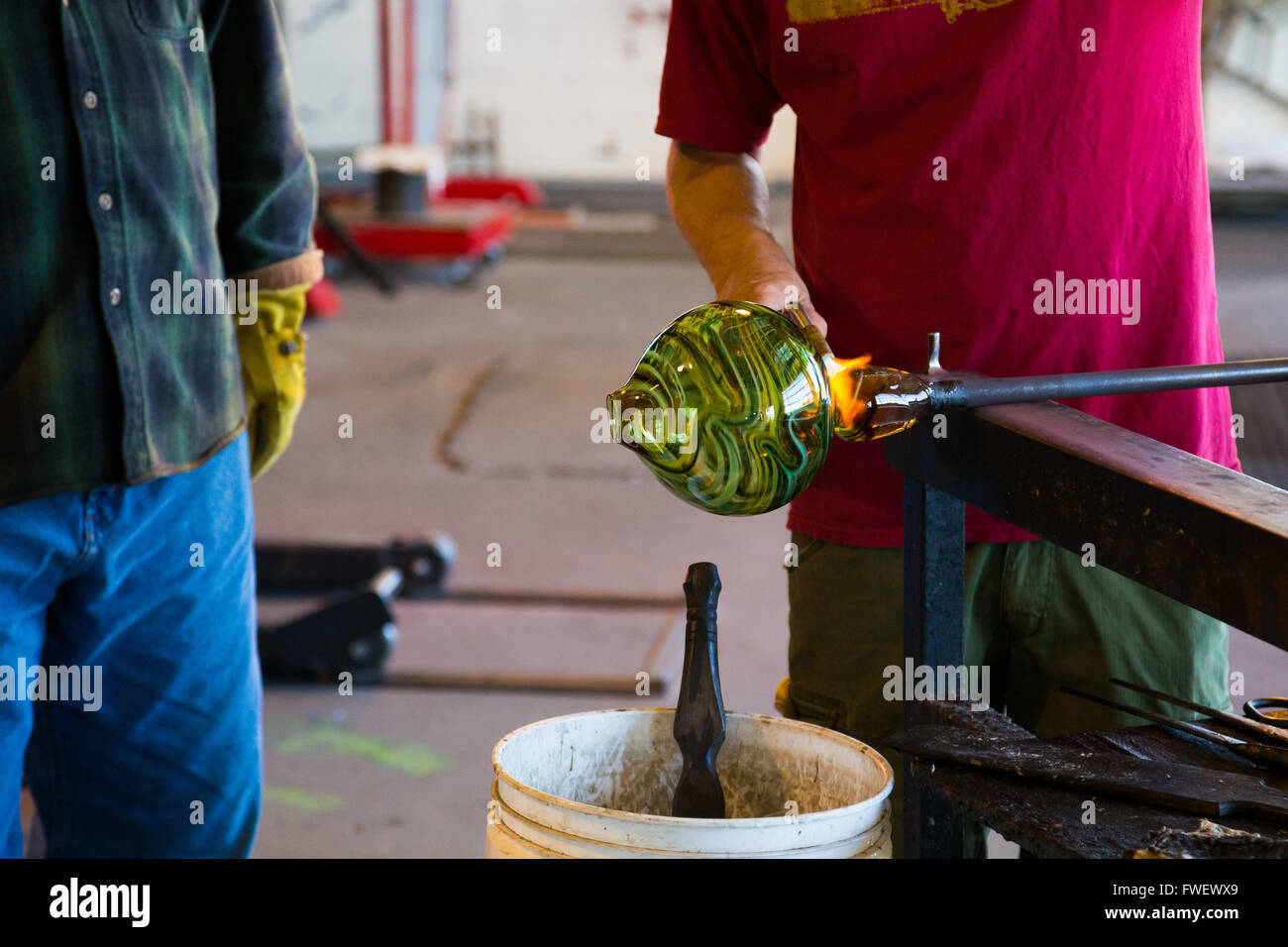 Two men are working hard to create a unique art piece of molten glass ...