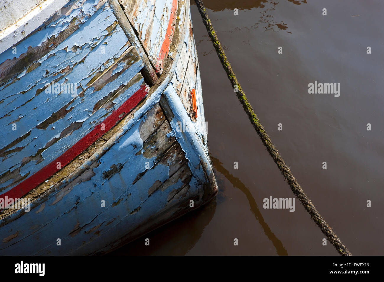 The hull of an old clinker built wooden fishing boat with flaking blue ...
