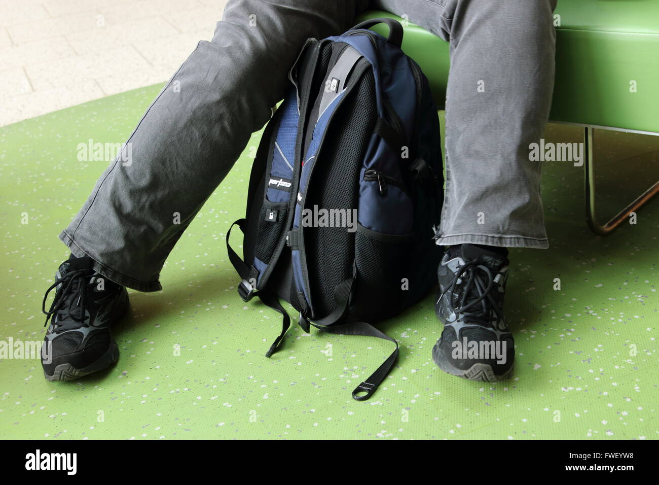 Male traveler sitting down on a bench with a backpack on the floor ...