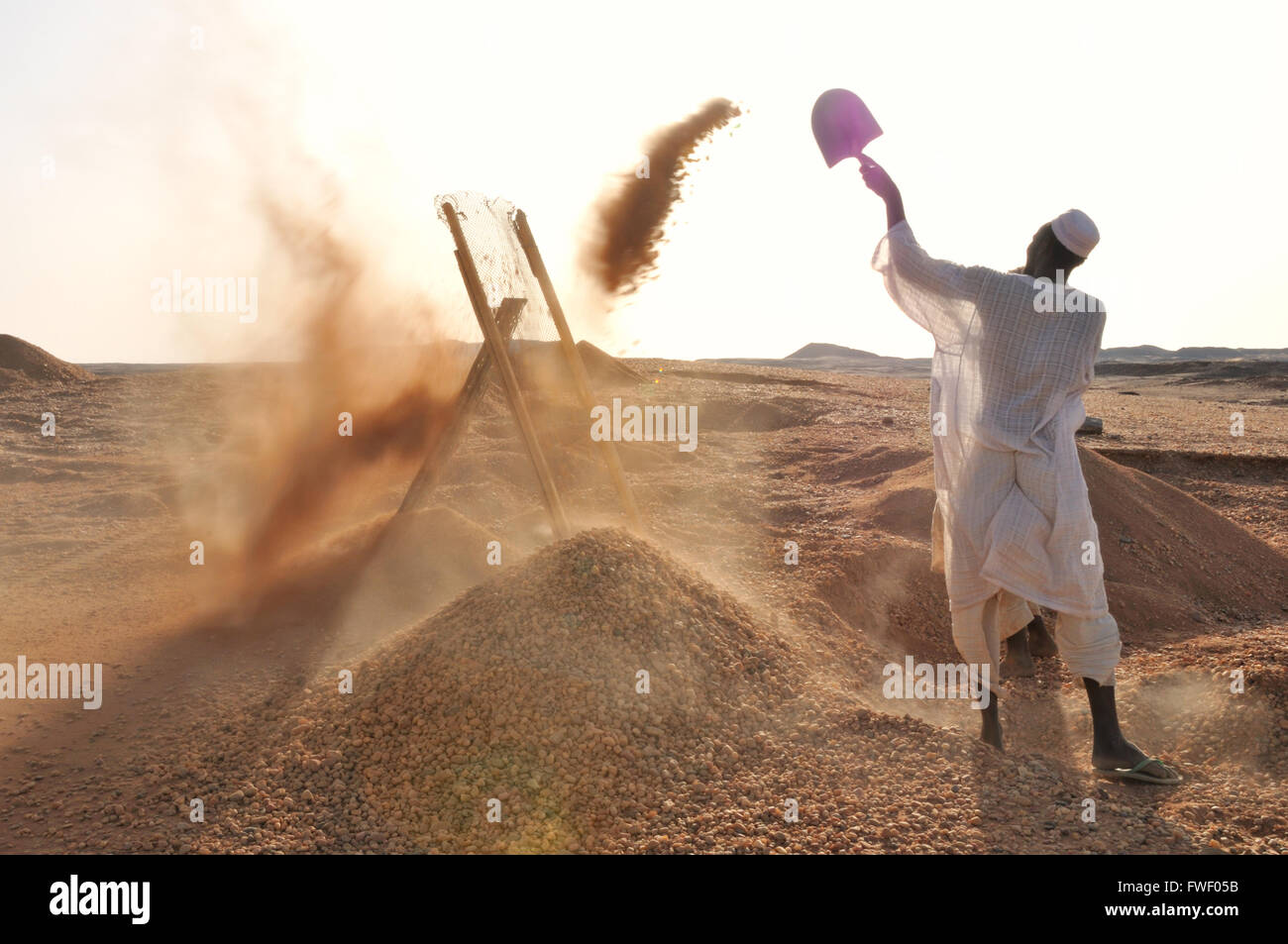 Man shoveling gravel at sunset Stock Photo - Alamy