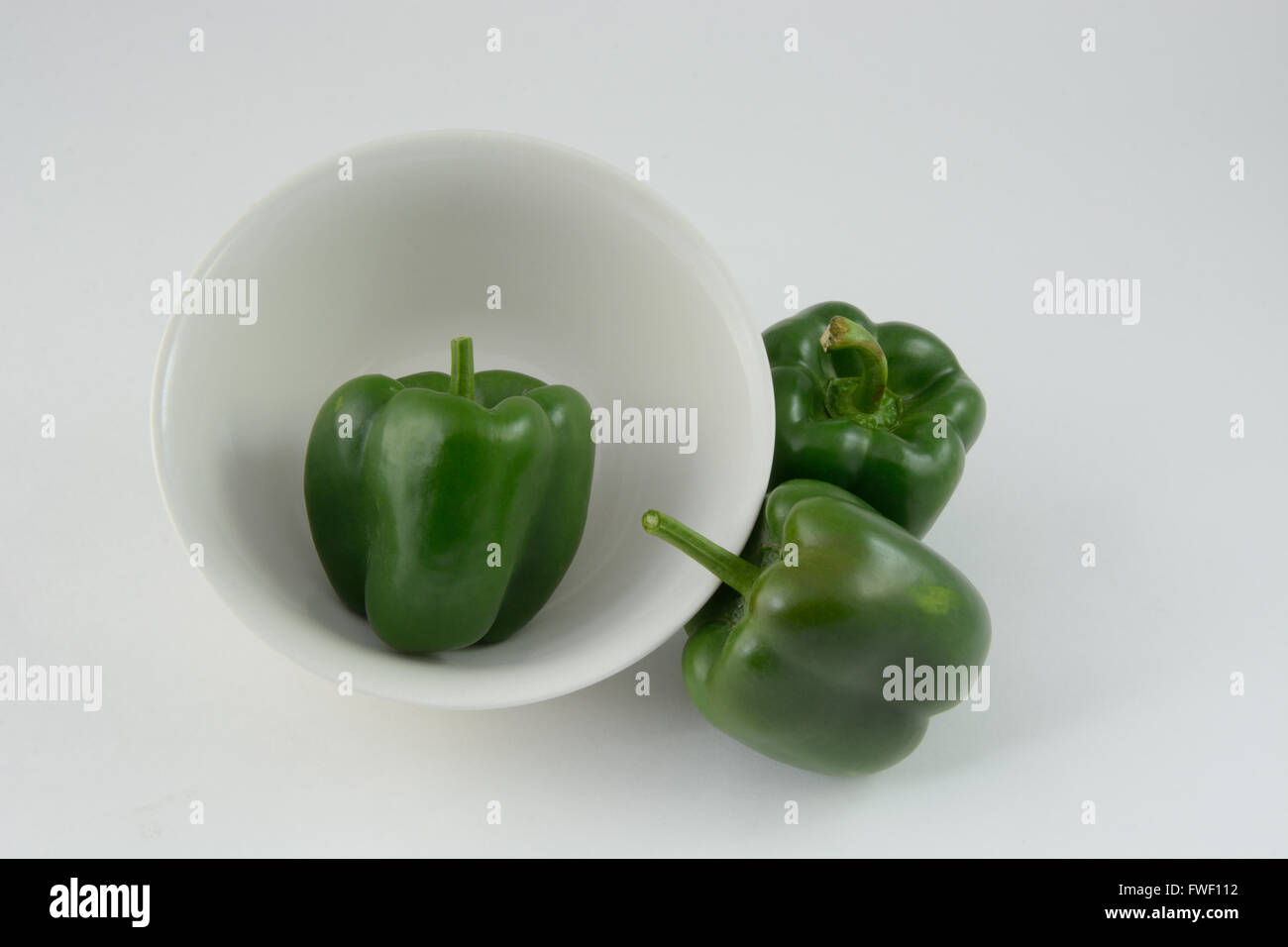 Green bell peppers inside and outside of white bowl Stock Photo - Alamy