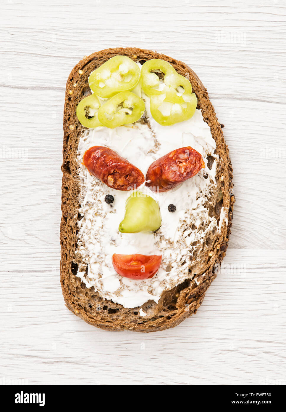 Funny face made of bread, butter, sausage, paprika, tomato and black ...
