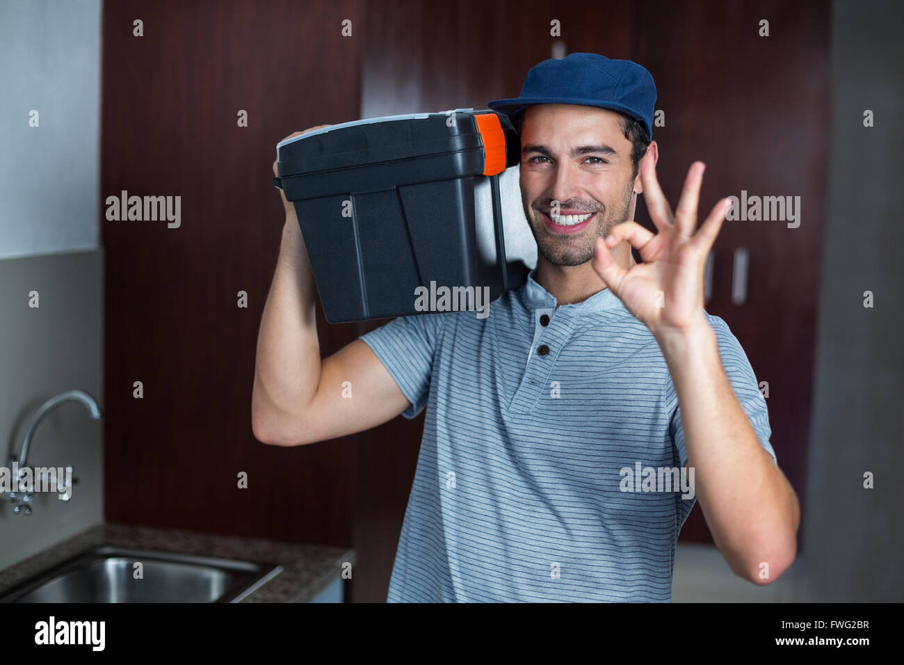 Smiling man carrying toolbox while showing ok sign Stock Photo - Alamy